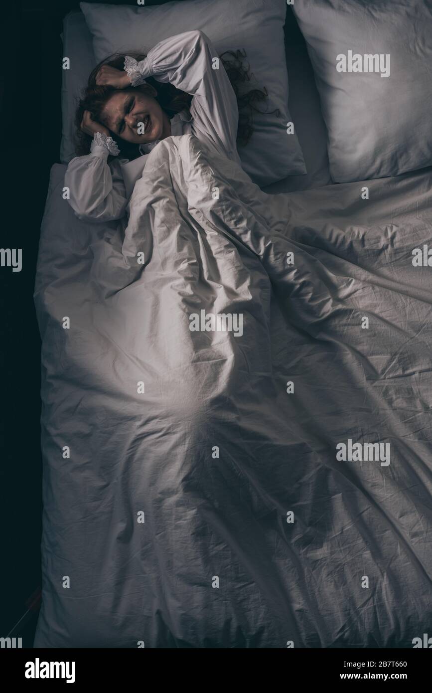 top view of paranormal girl in nightgown with headache lying in bed ...