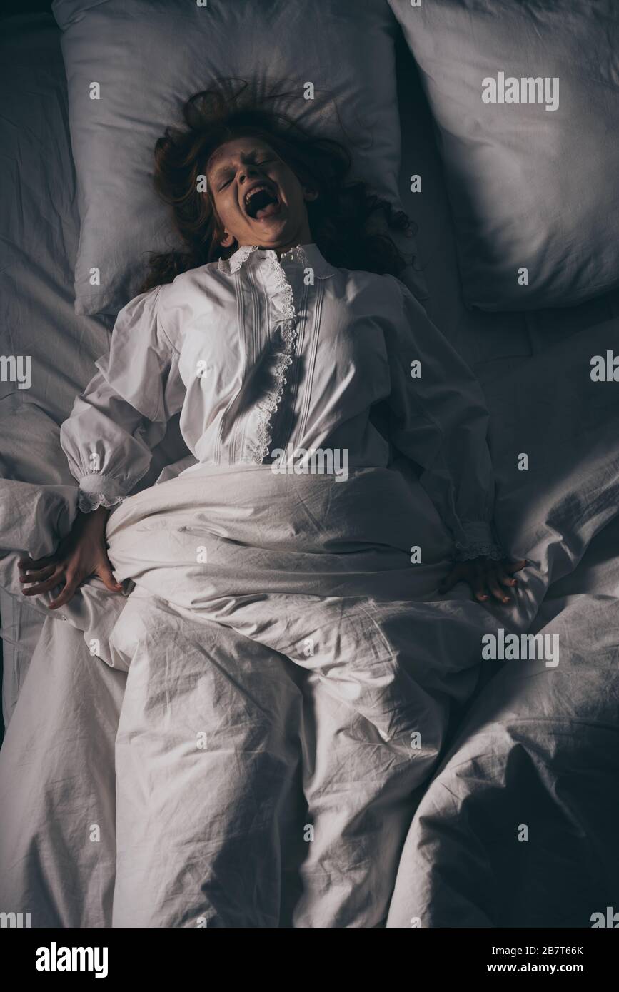 top view of demoniacal evil girl in nightgown screaming while lying in ...