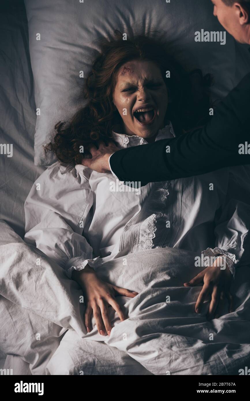 exorcist holding screaming obsessed girl in bed Stock Photo - Alamy