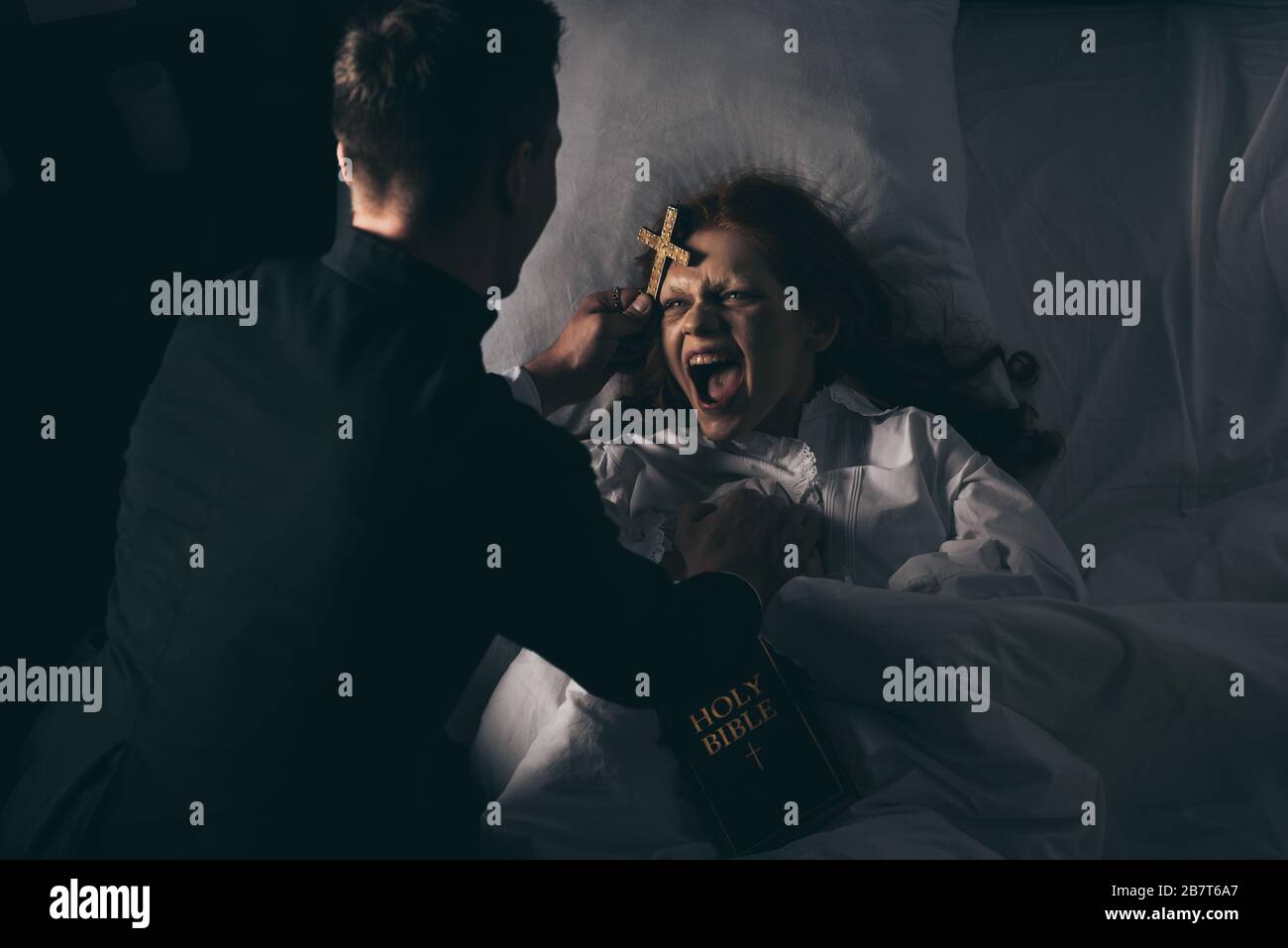 male exorcist with bible and cross standing over demoniacal screaming ...