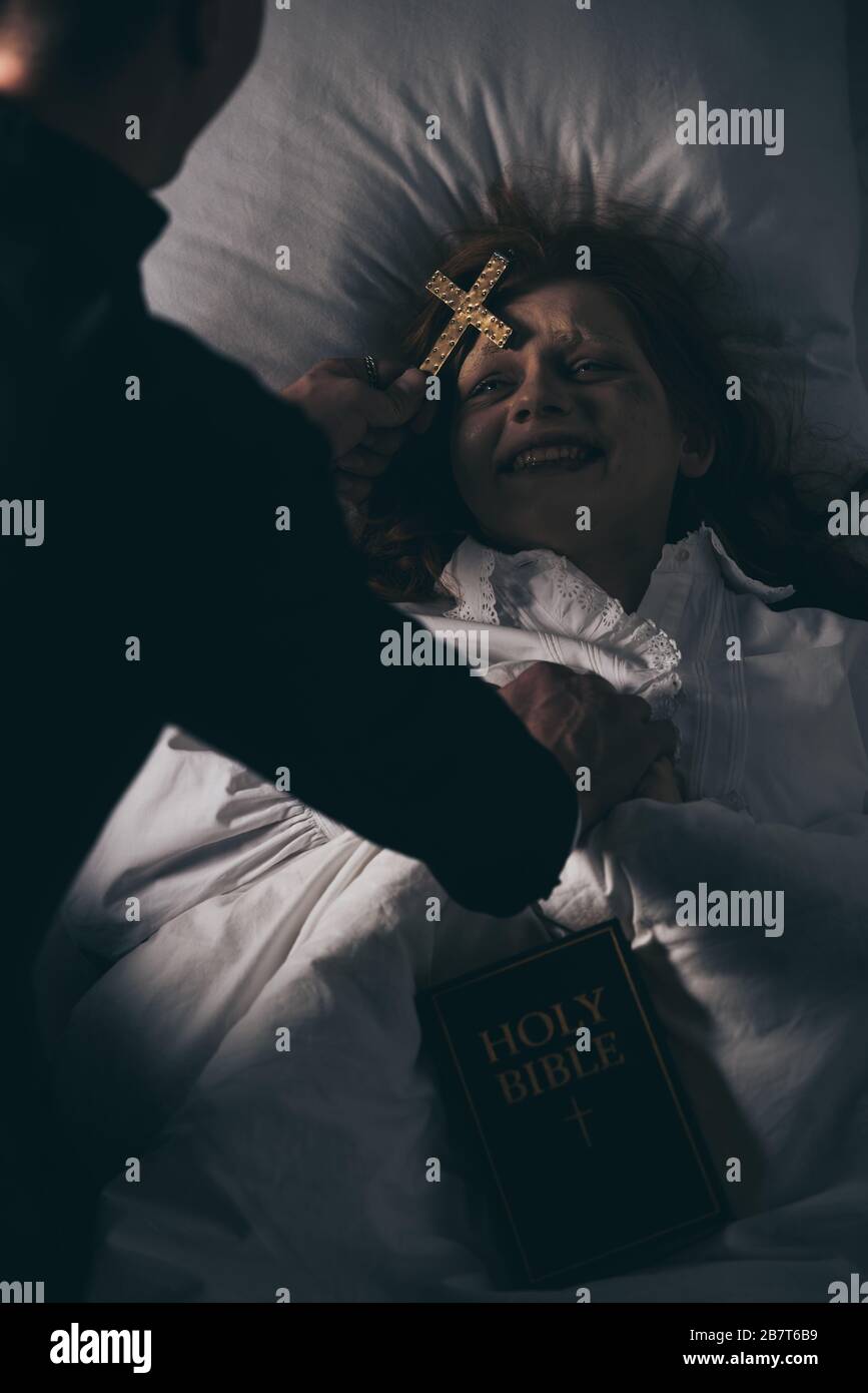 exorcist with bible and cross standing over demoniacal girl in bed ...