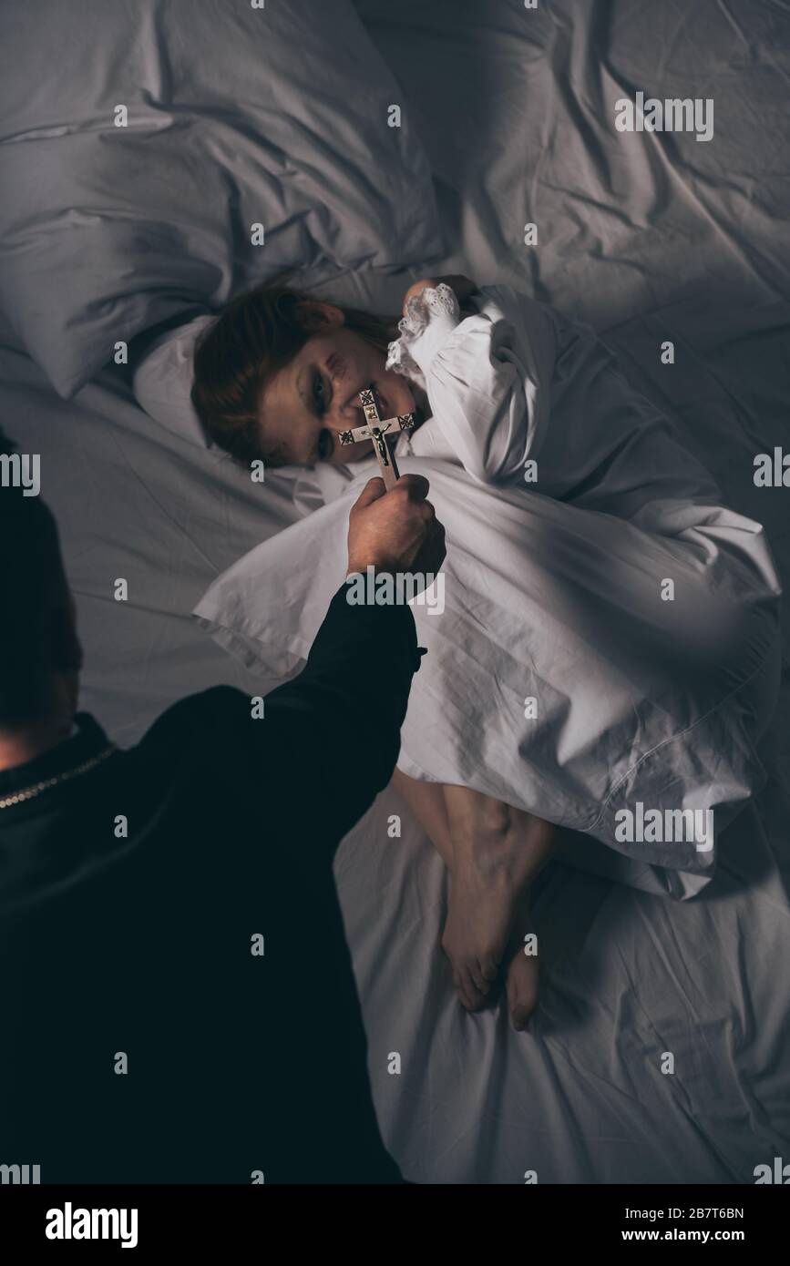 exorcist holding cross over female demon in bed Stock Photo - Alamy