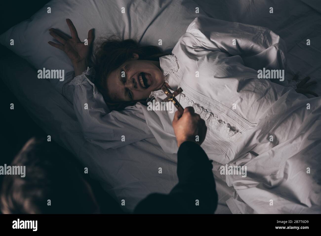 exorcist holding cross over demonic yelling girl in bed Stock Photo - Alamy
