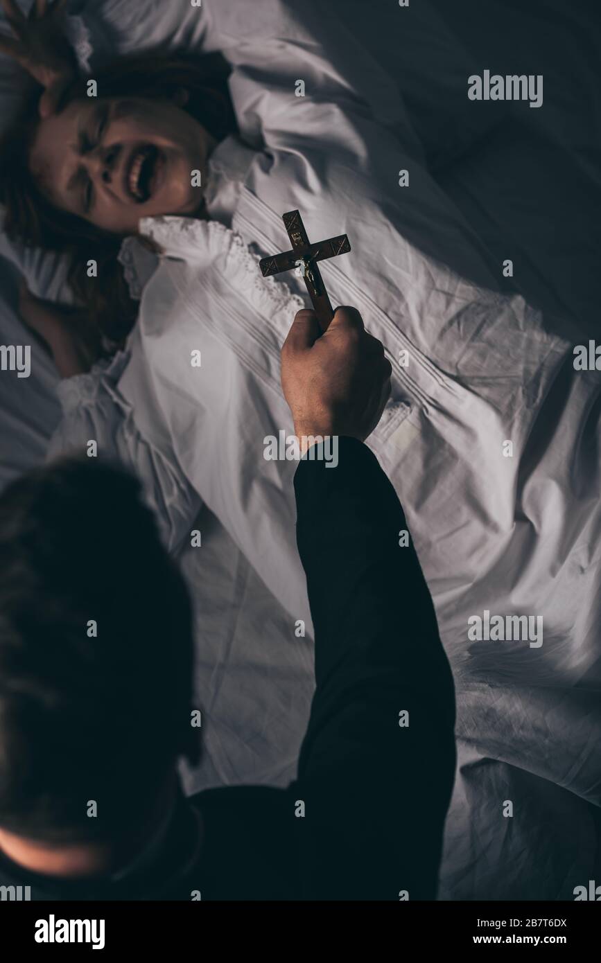 exorcist holding cross over obsessed screaming girl in bed Stock Photo ...