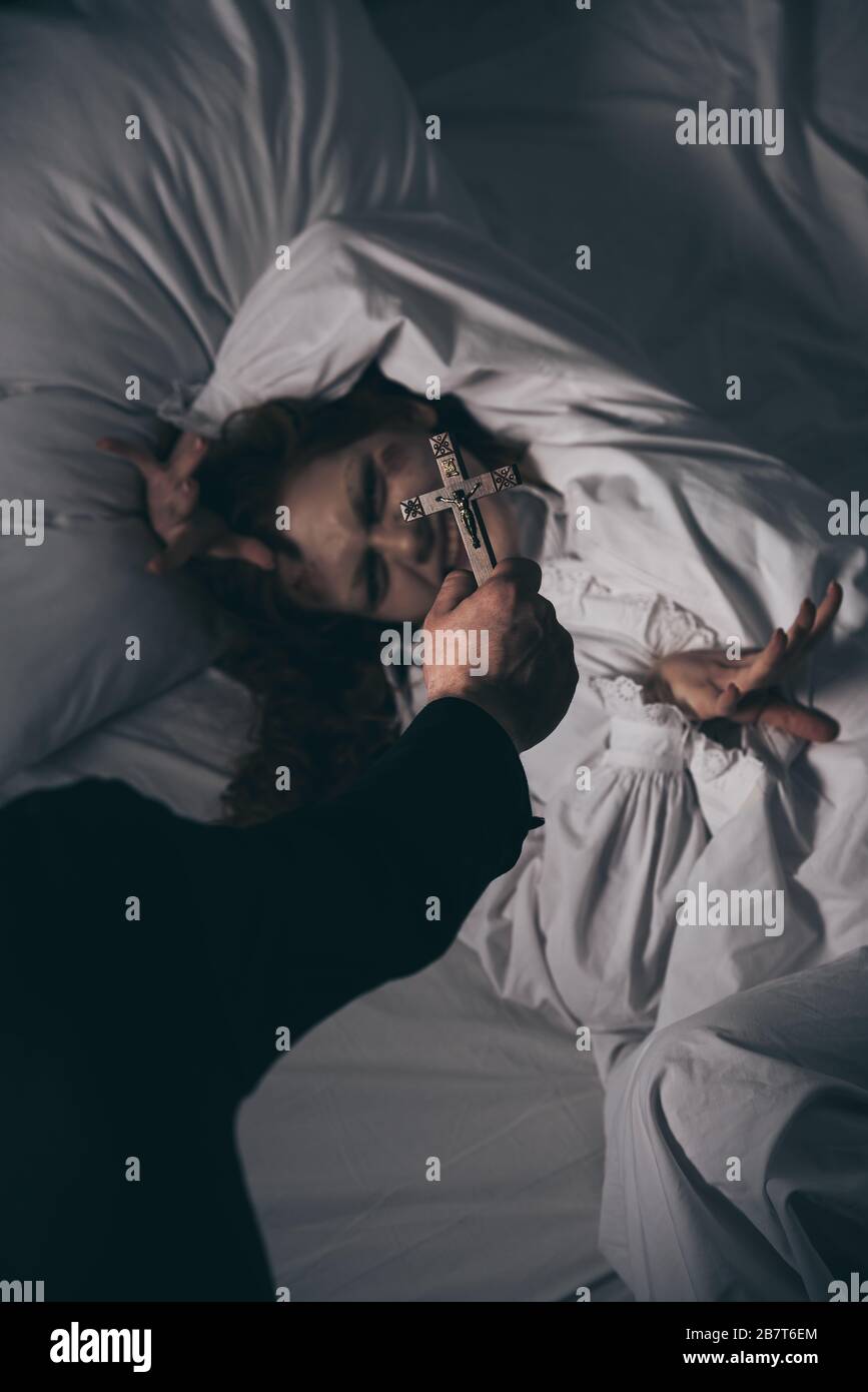 exorcist holding cross over female demon in bed Stock Photo - Alamy