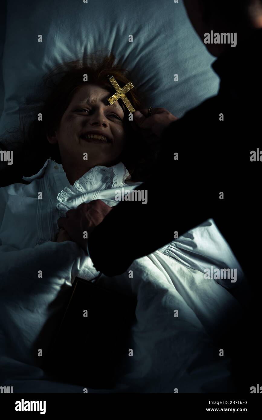 exorcist holding cross over female demon in bed Stock Photo - Alamy