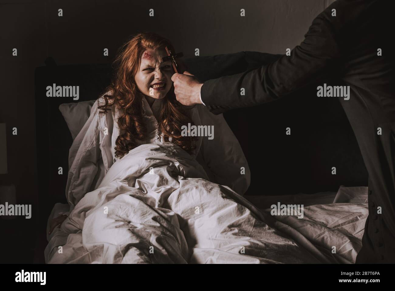exorcist holding cross in front of obsessed girl in bed Stock Photo - Alamy