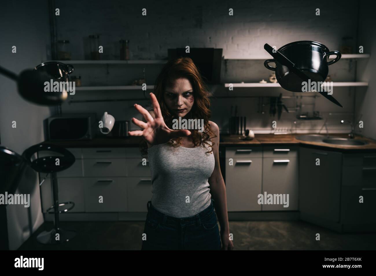 concentrated demoniacal girl with levitating kitchenware in kitchen ...