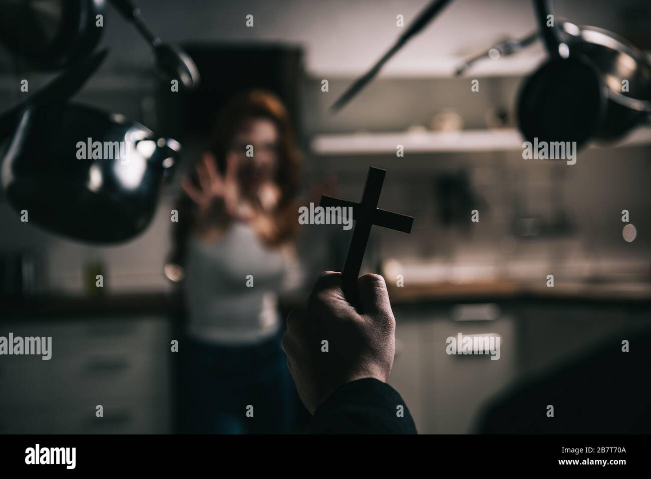 selective focus of female demon with levitating cookware and exorcist ...