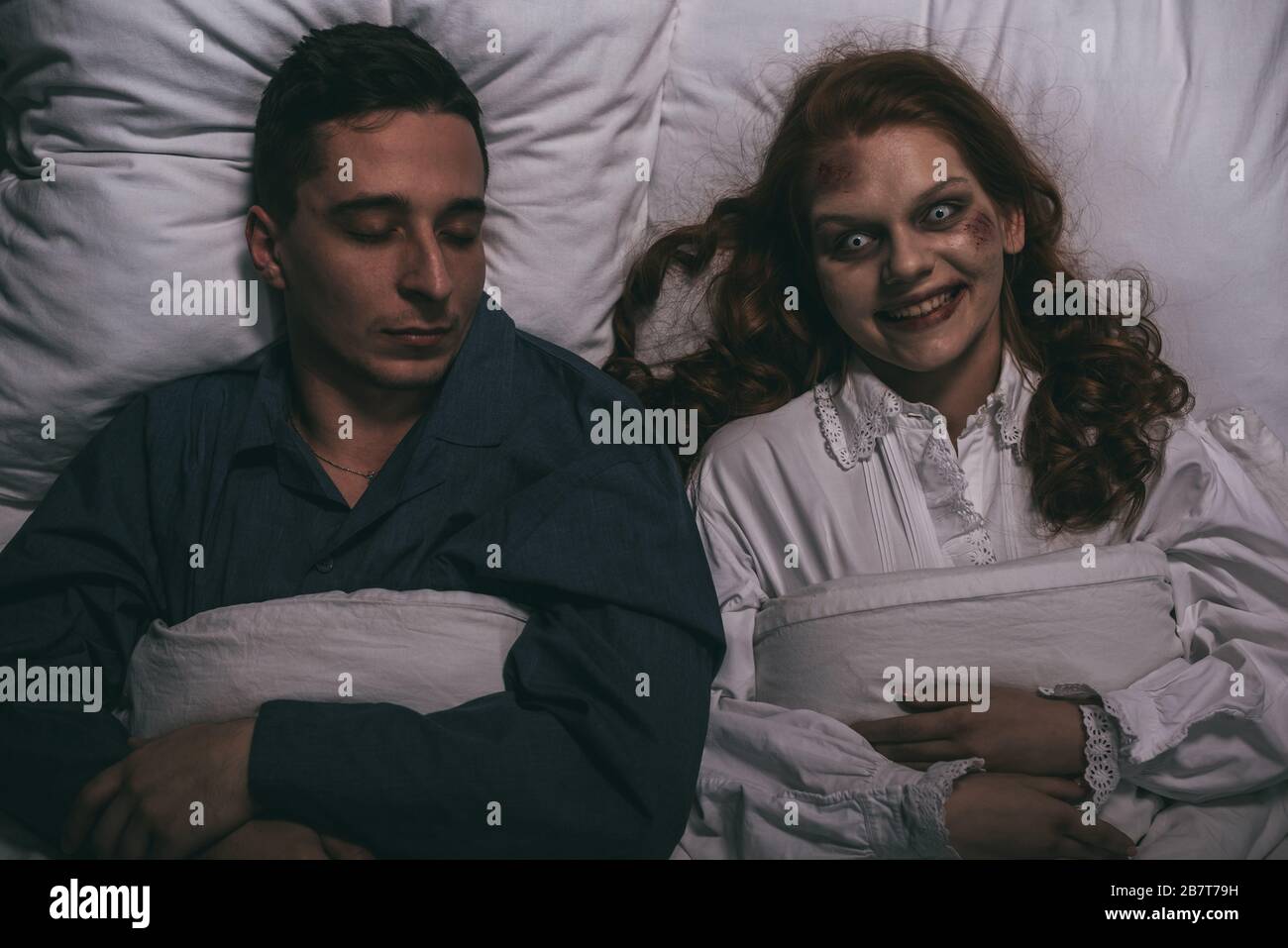 top view of creepy smiling female demon lying in bed with sleeping man ...