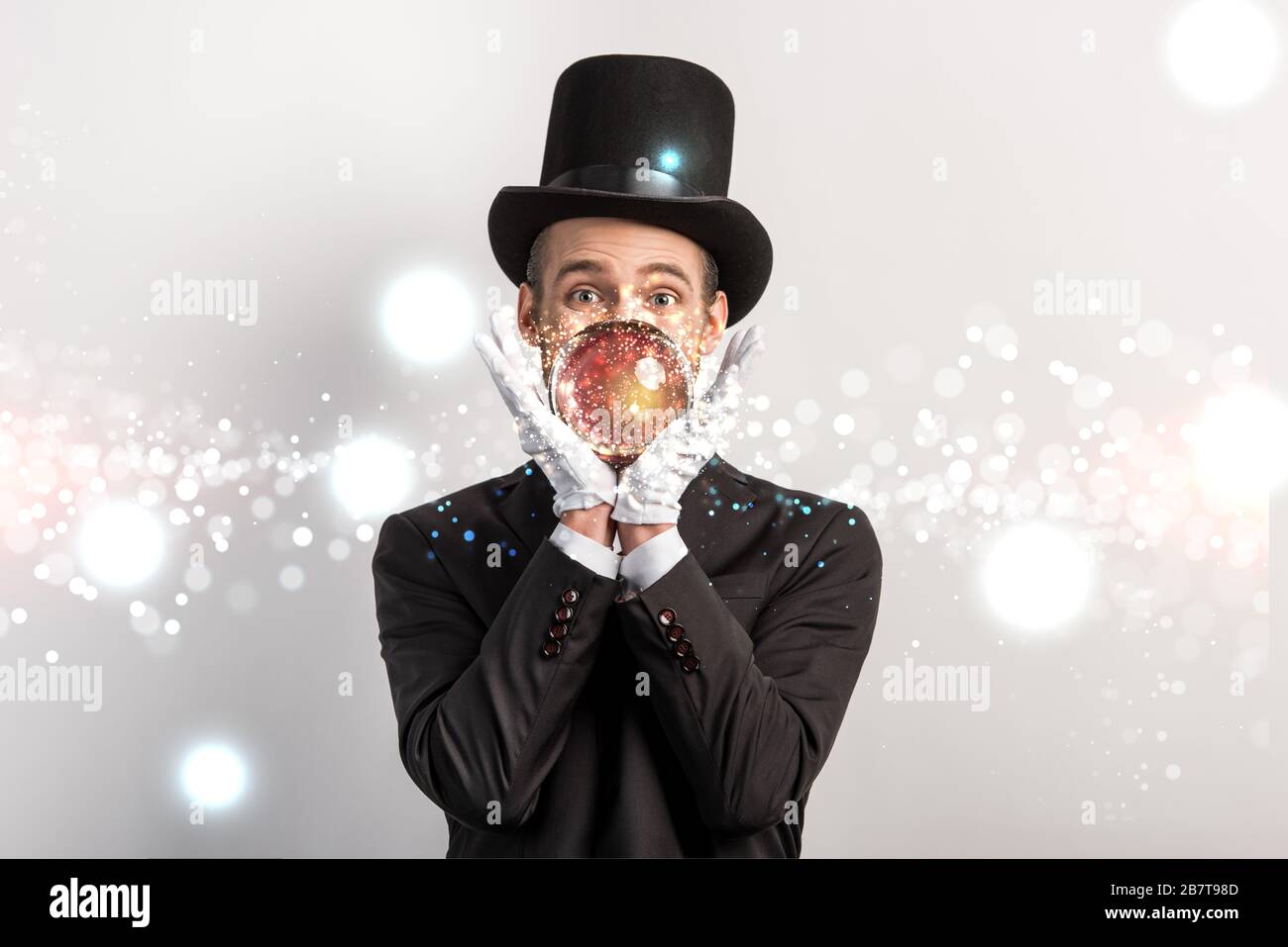 professional magician holding magic ball isolated on grey with glowing ...