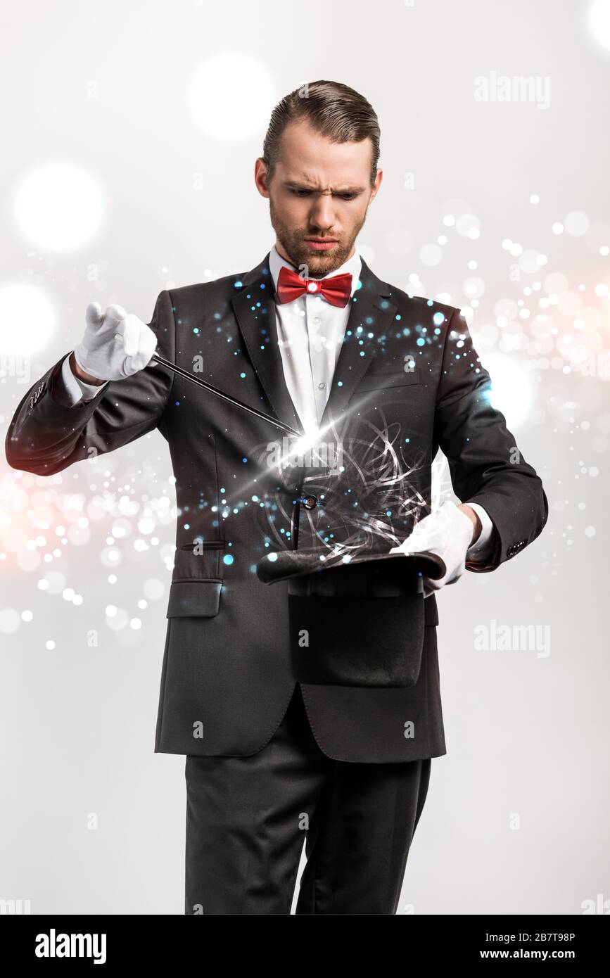 confused magician in suit making trick hat and wand isolated on grey ...