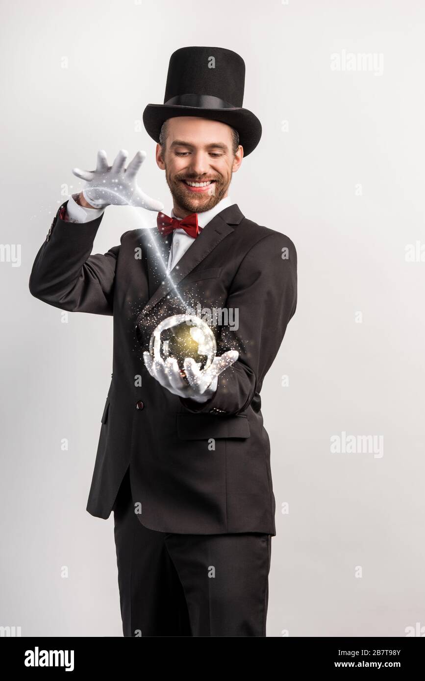 happy professional magician holding magic ball isolated on grey with ...