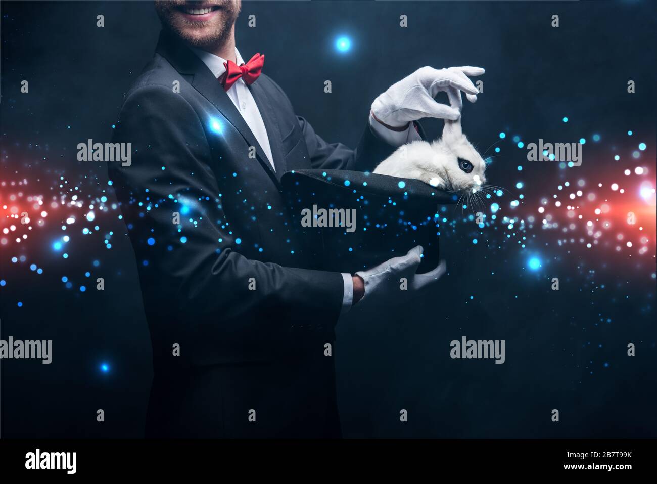 cropped view of smiling magician showing trick with white rabbit in hat ...