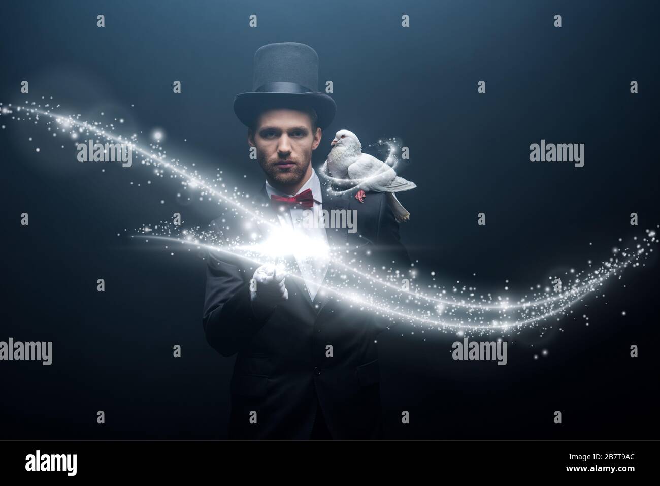 dove sitting on shoulder of young magician in hat with wand in dark ...