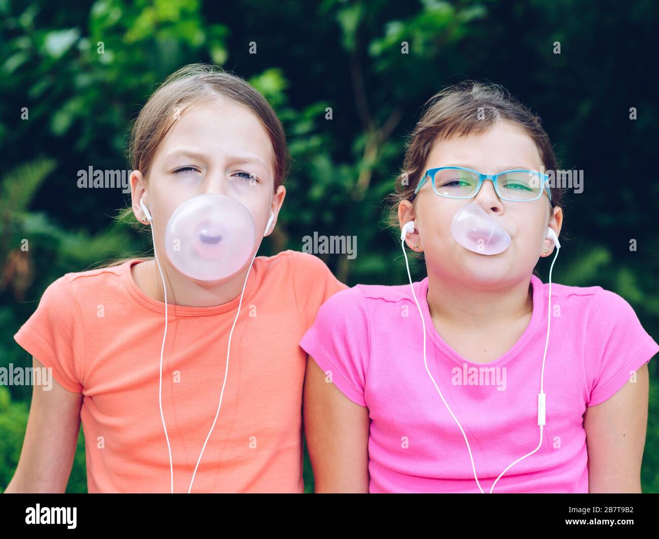 Girls sharing headphones to listen to music. The sisters chew gum and ...