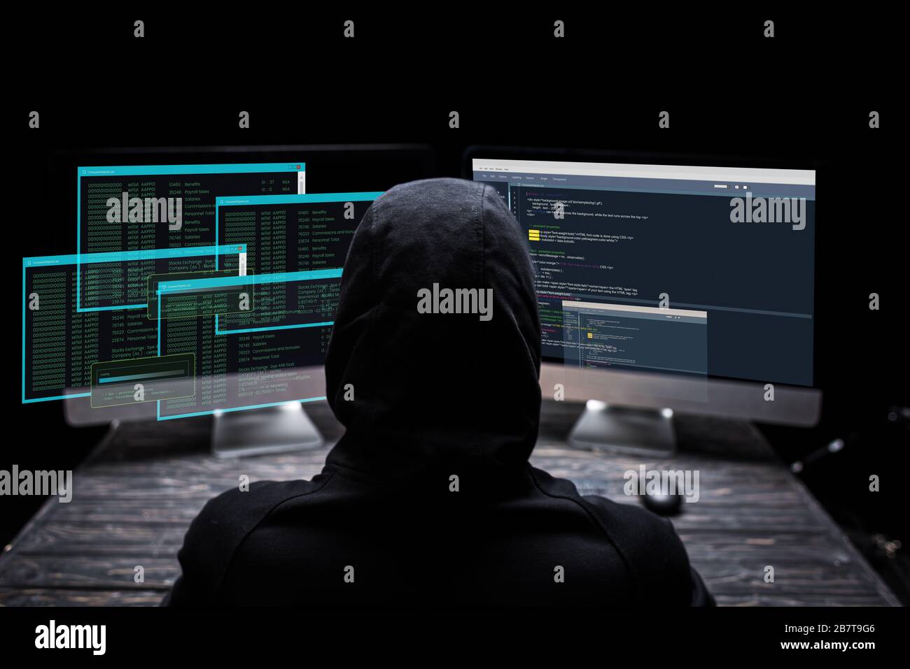 back view of hooded hacker sitting near computer monitors with data on ...
