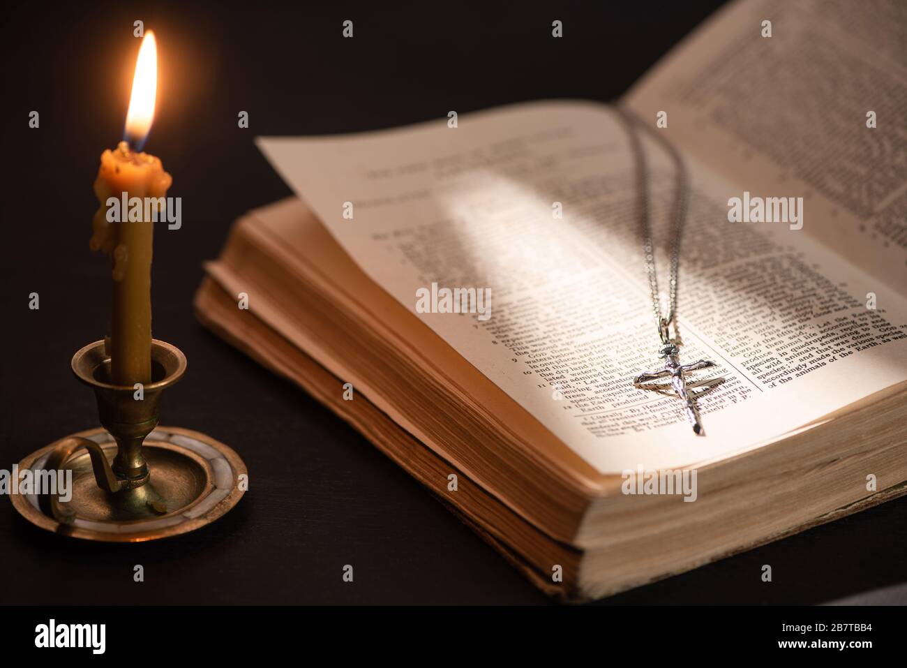 church candle in candlestick burning near bible with catholic cross in ...