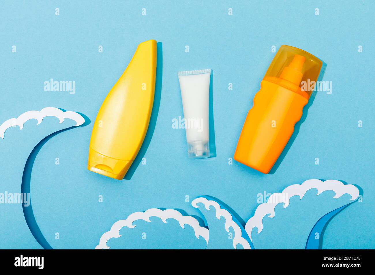Top view of tubes and dispenser bottle of sunscreen with paper cut sea ...