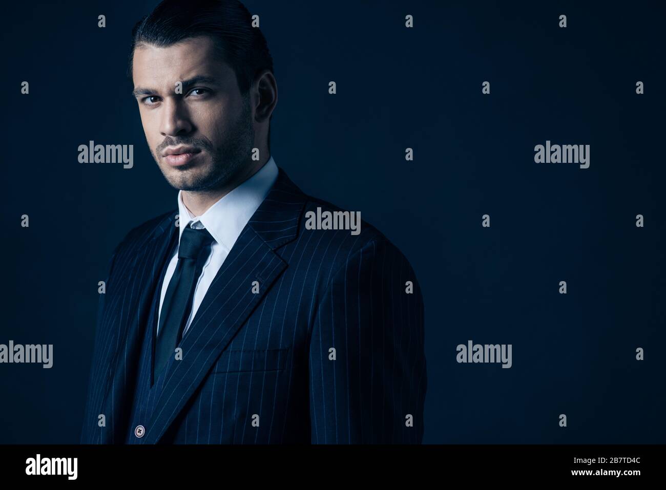 Elegant mafioso looking at camera on dark blue background Stock Photo ...
