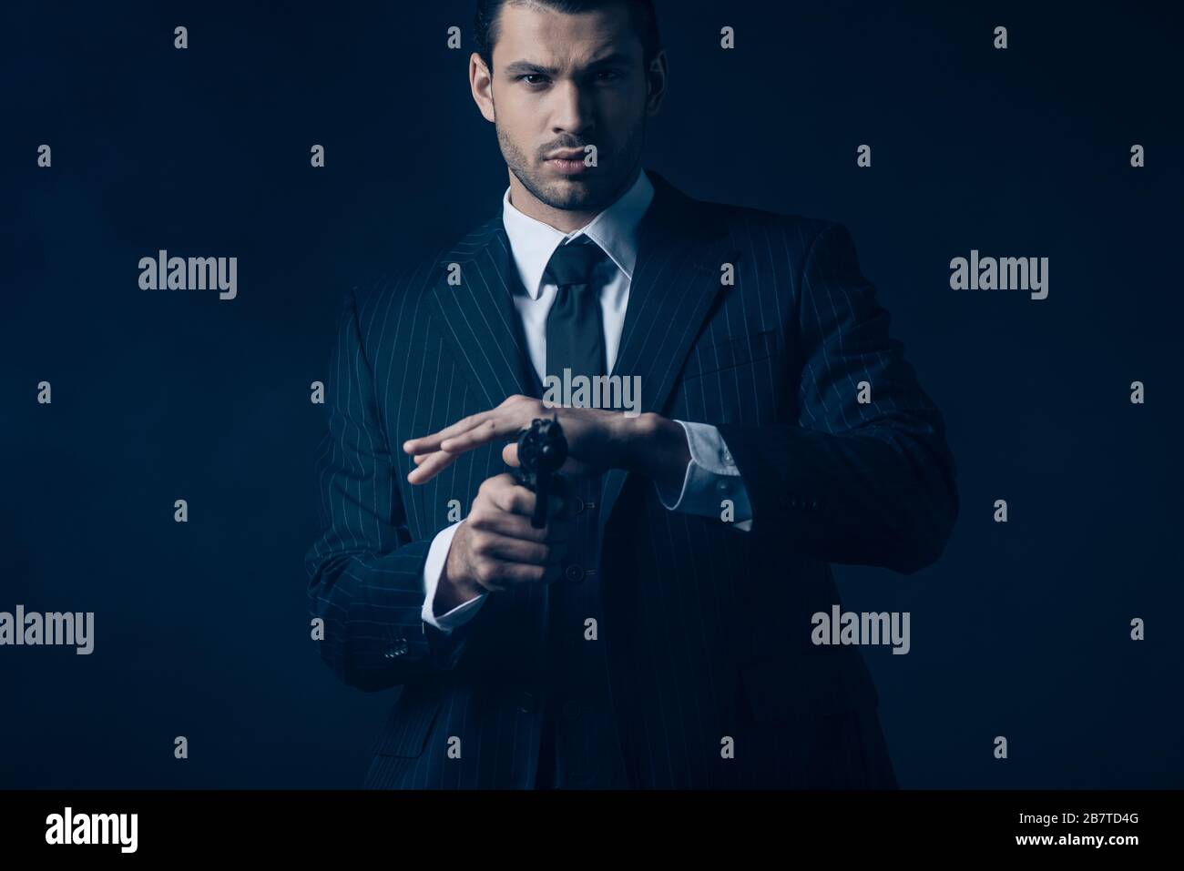 Front view of gangster aiming gun barrel and looking at camera on dark ...