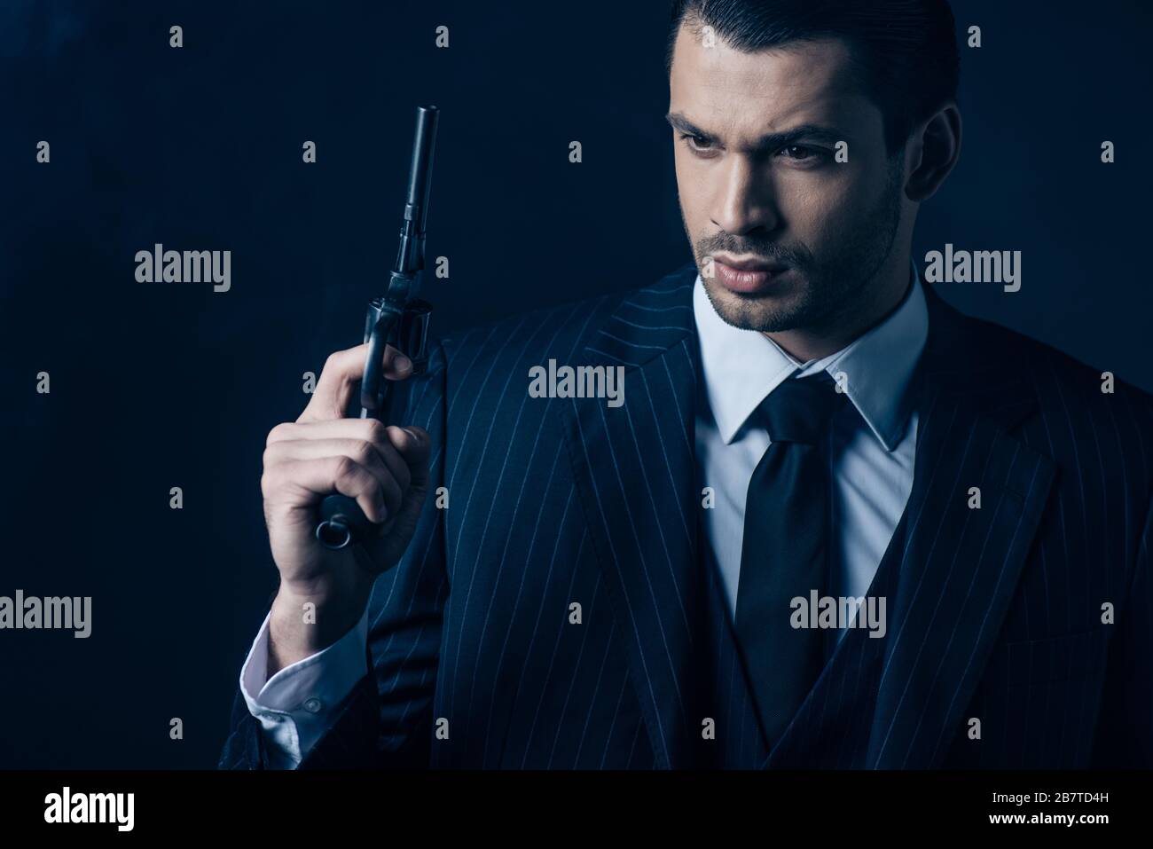 Pensive gangster raising gun on dark blue background Stock Photo - Alamy