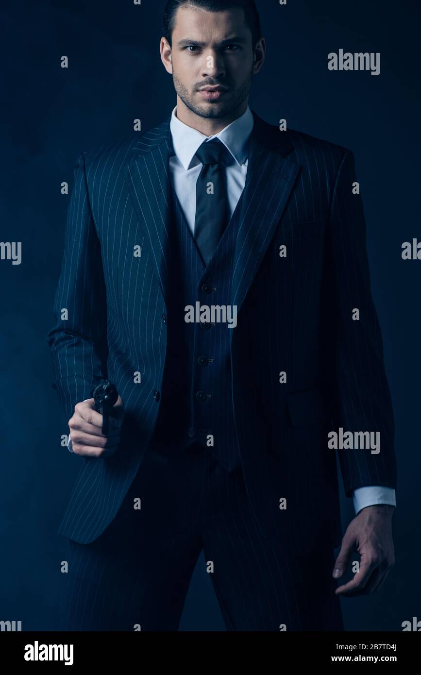 Front view of confident gangster aiming weapon and looking at camera on ...