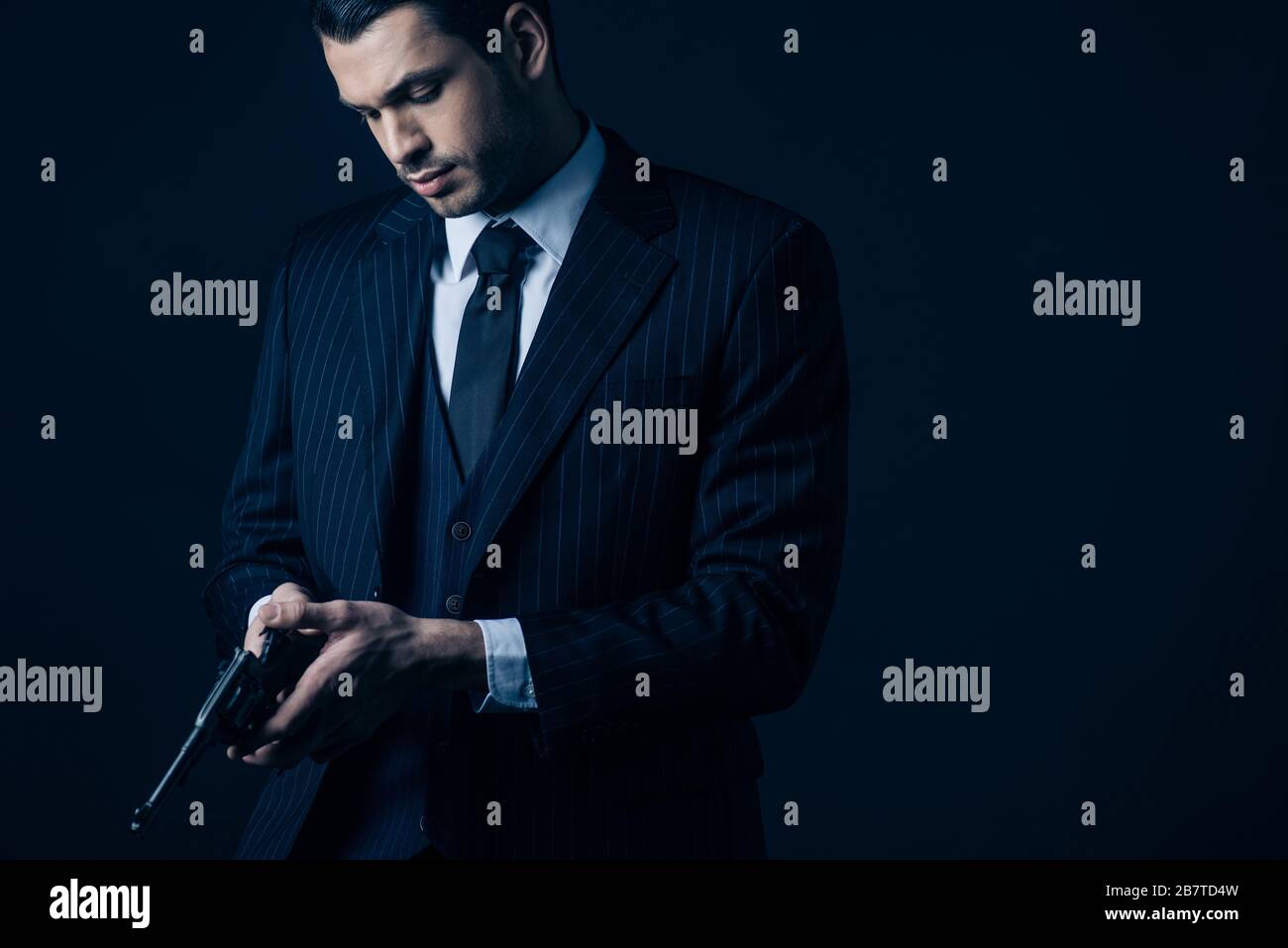 Gangster in elegant suit loading revolver on black background Stock ...
