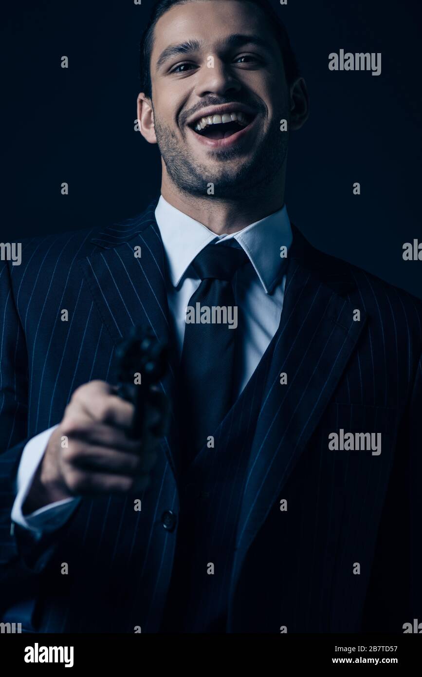 Selective focus of gangster aiming gun, laughing and looking at camera ...