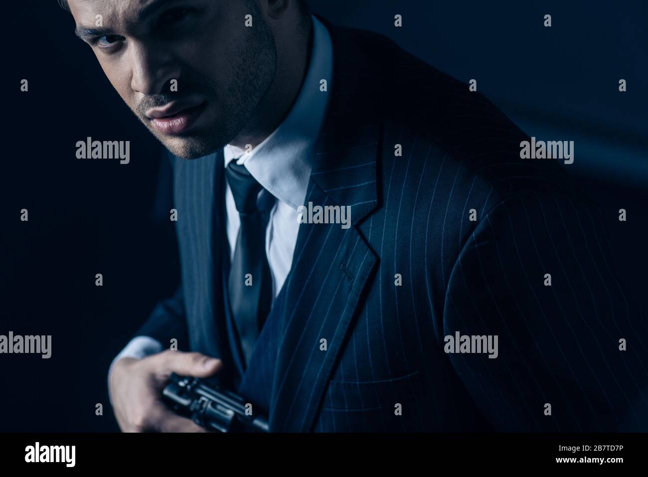 Gangster with revolver looking at camera with suspicion on dark ...