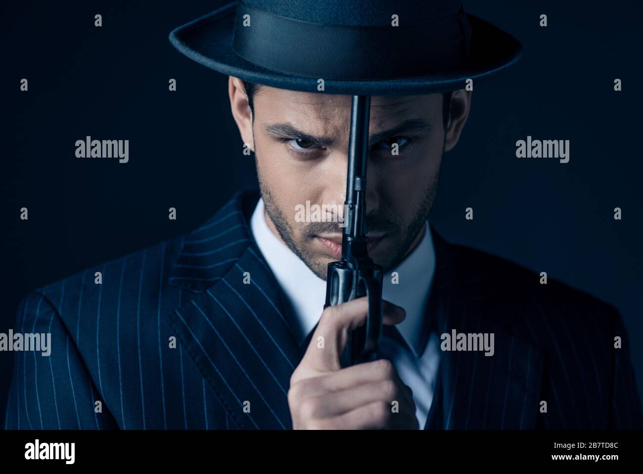 Portrait of gangster holding gun in front of face on dark blue Stock ...