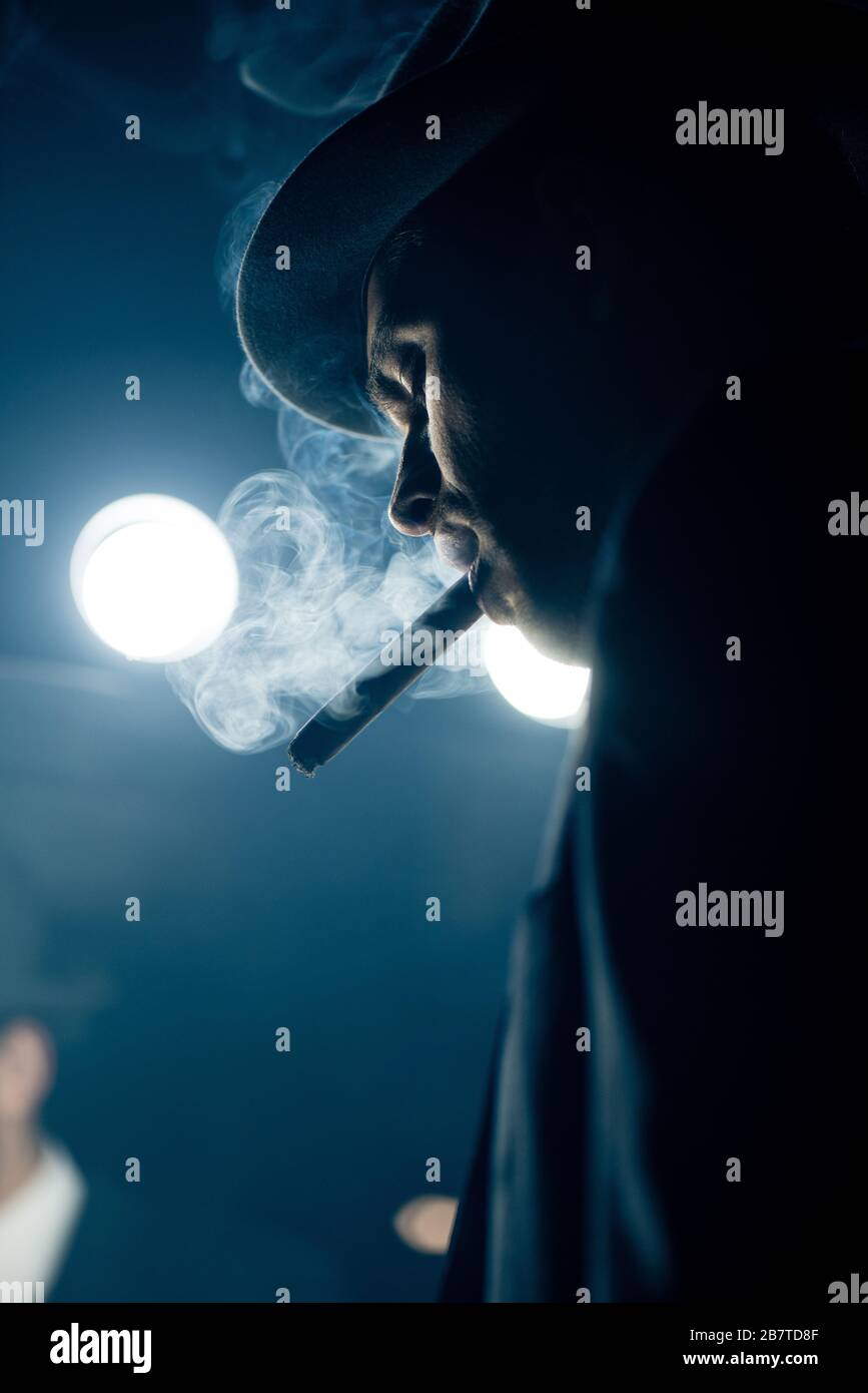 Low angle view of mafioso smoking cigar on dark Stock Photo - Alamy