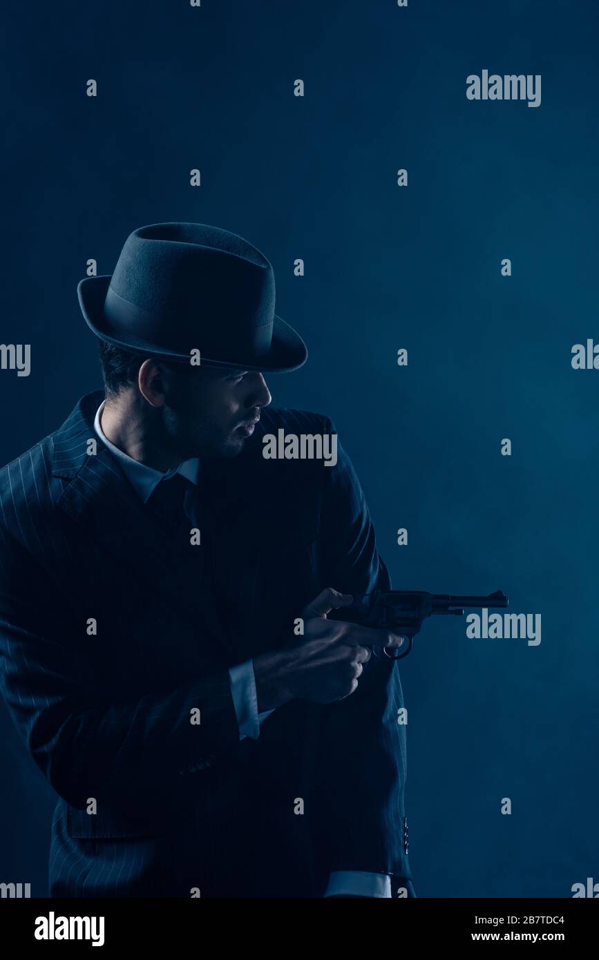 Gangster holding gun and aiming on dark blue background Stock Photo - Alamy