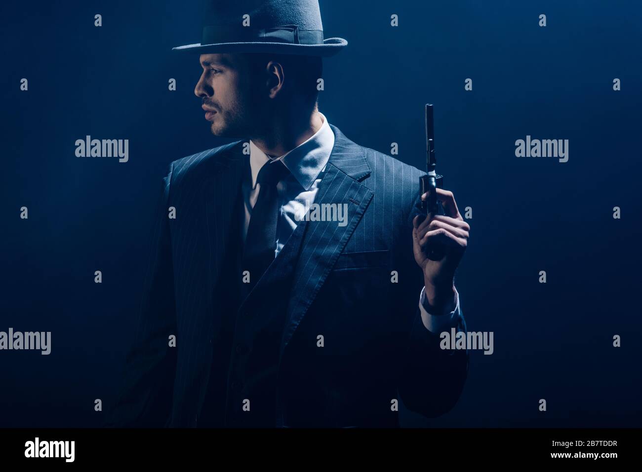 Gangster raising revolver and looking away on dark background Stock ...