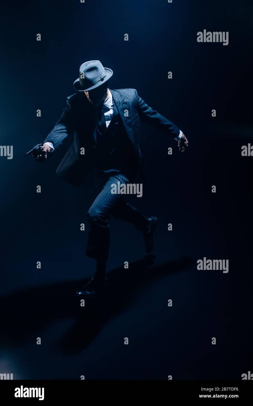 Gangster with outstretched hand aiming weapon and running on dark Stock ...