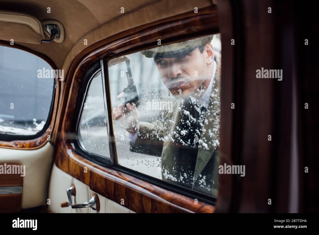 Selective focus of mafioso with gun looking inside retro car Stock ...