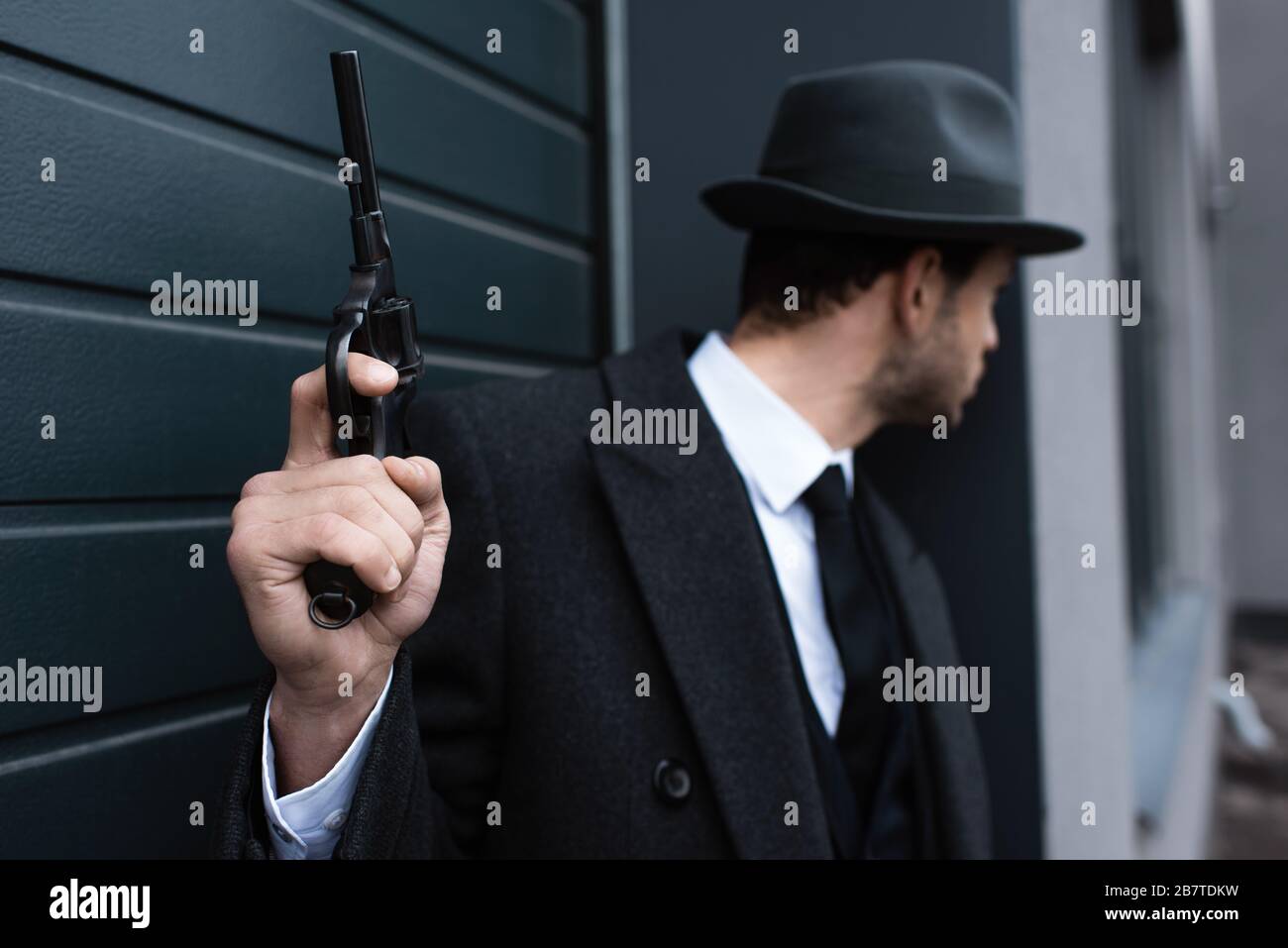 Selective focus of mafioso holding gun in corner on street Stock Photo ...