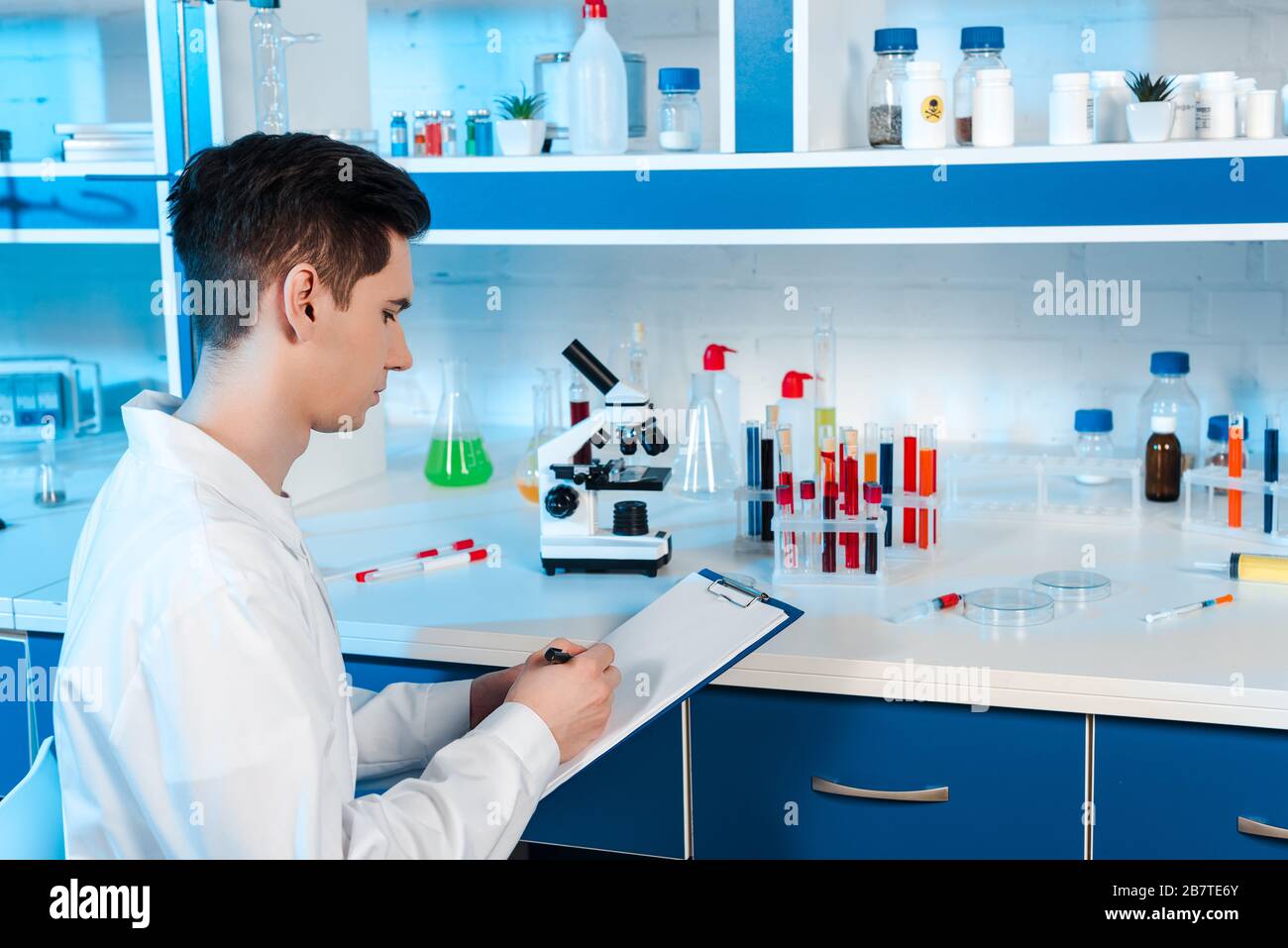 handsome scientist writing near microscope and test tubes Stock Photo ...