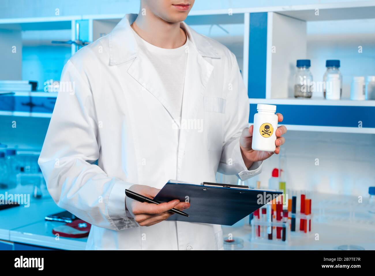 cropped view of scientist holding clipboard and bottle with toxic ...