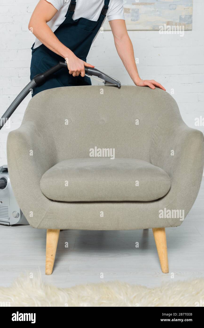 cropped view of cleaner in uniform dry cleaning armchair with vacuum ...