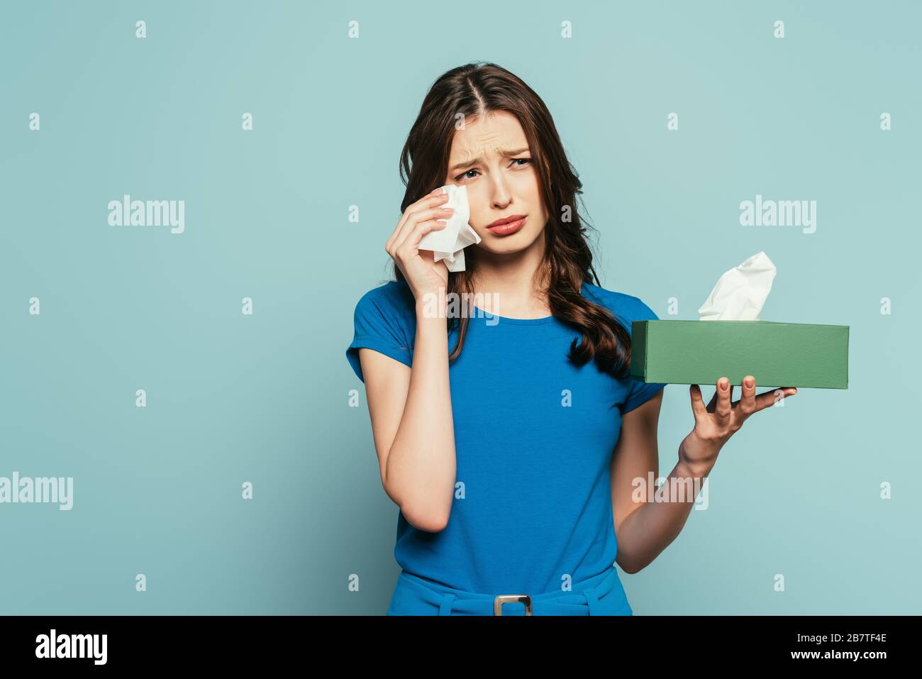 sad girl wiping tears with paper napkin while crying isolated on blue ...