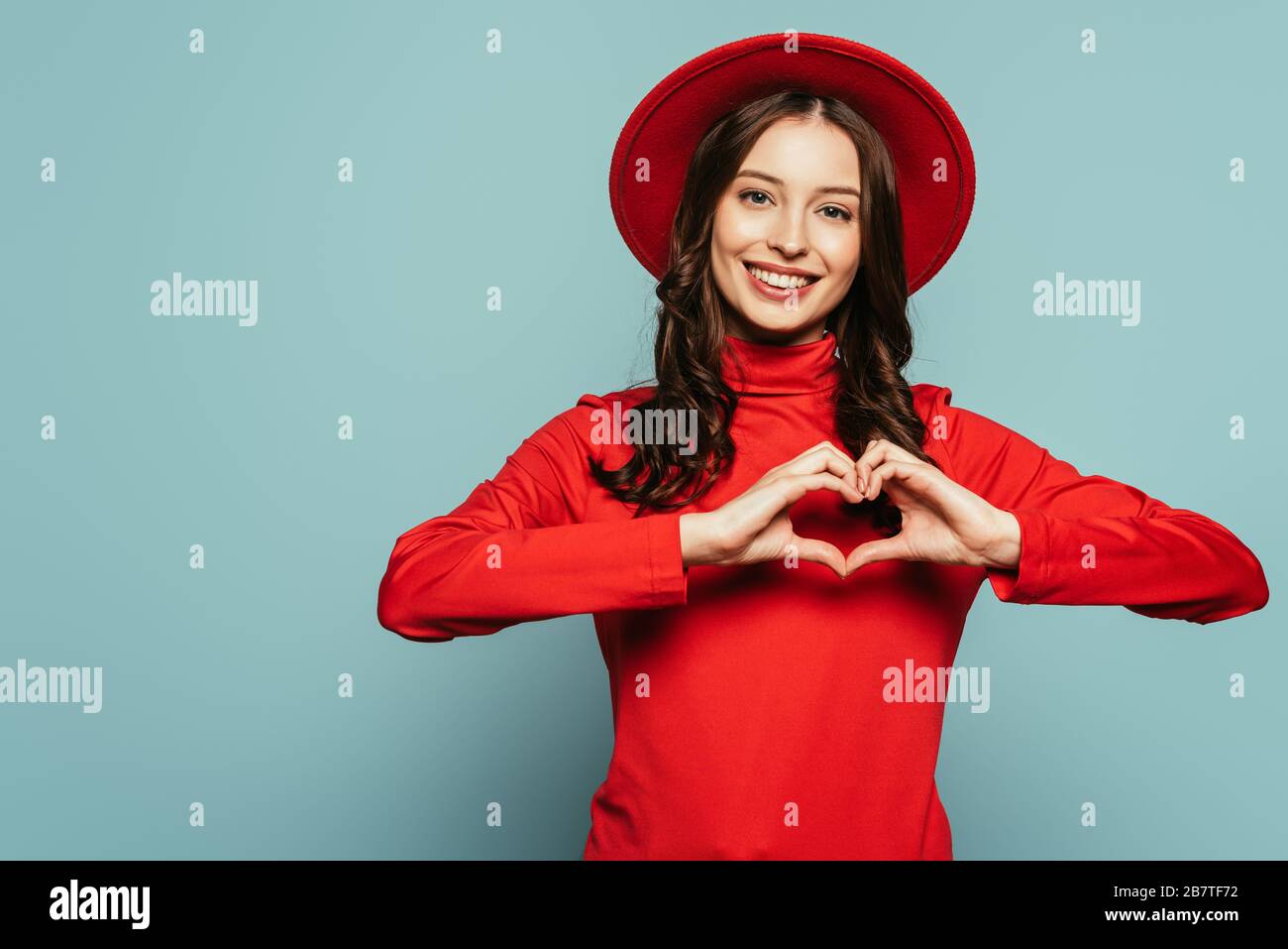 happy stylish girl showing heart symbol with hands on blue background ...