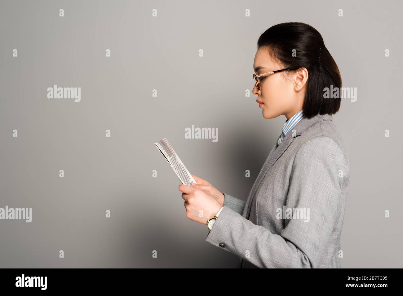 side view of young businesswoman in eyeglasses reading newspaper on ...