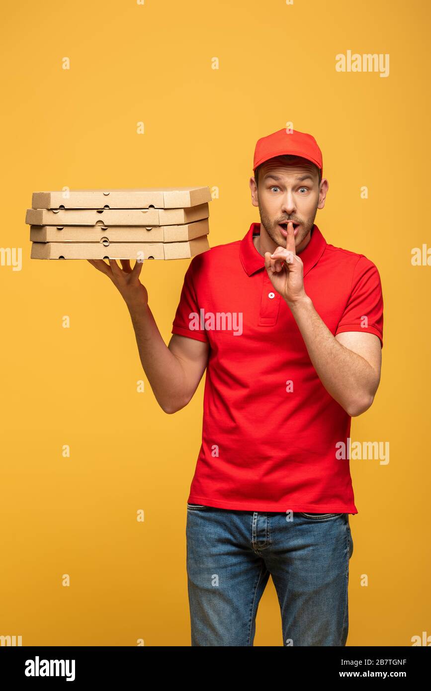 shocked delivery man in red uniform holding pizza boxes and showing shh ...