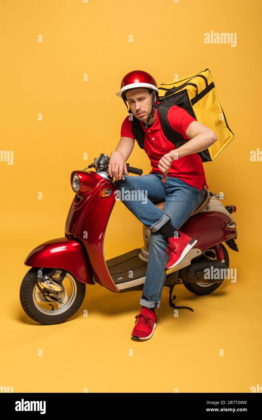 sad delivery man with backpack on scooter showing thumb down on yellow ...