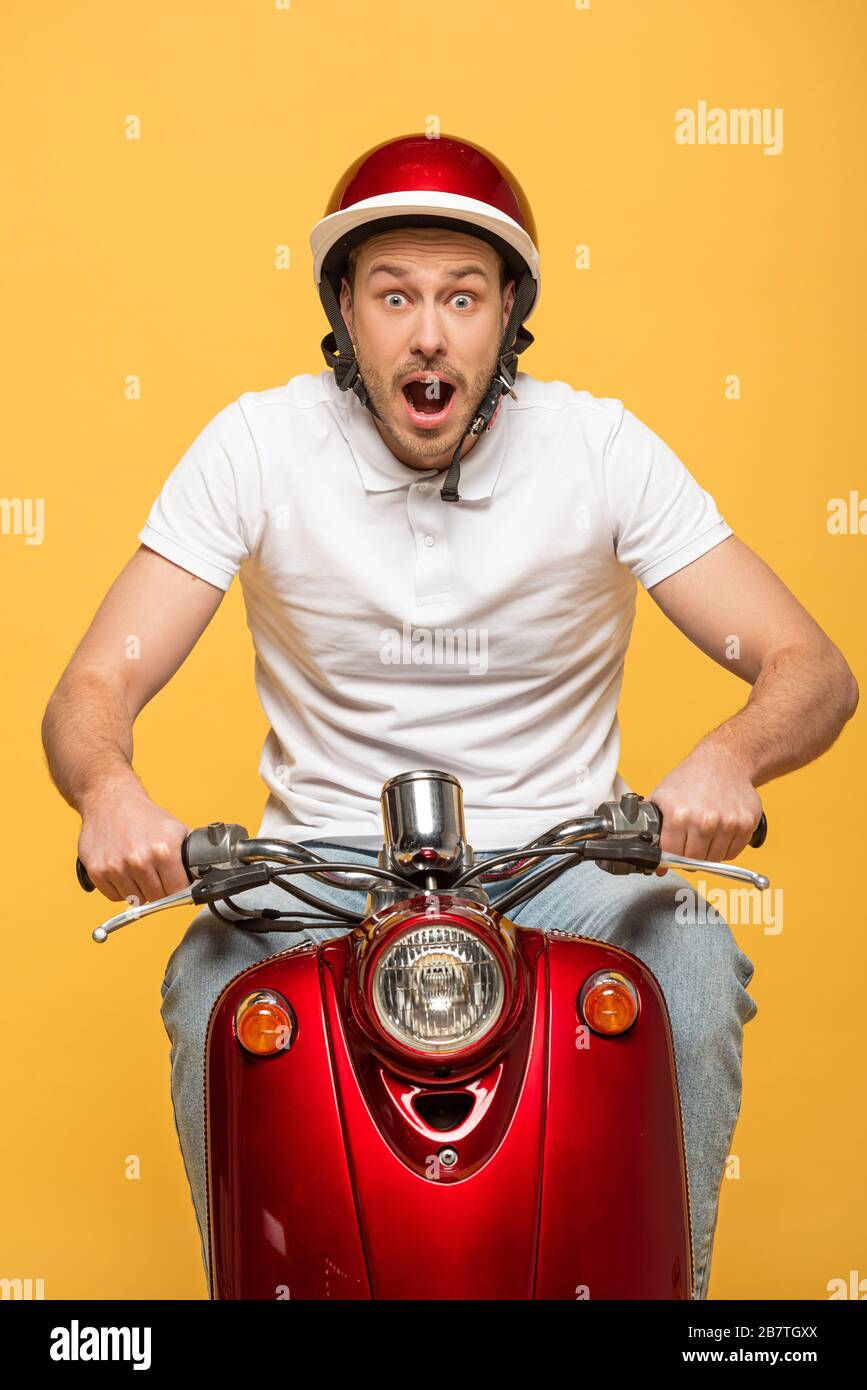 shocked delivery man in helmet riding scooter isolated on yellow Stock ...