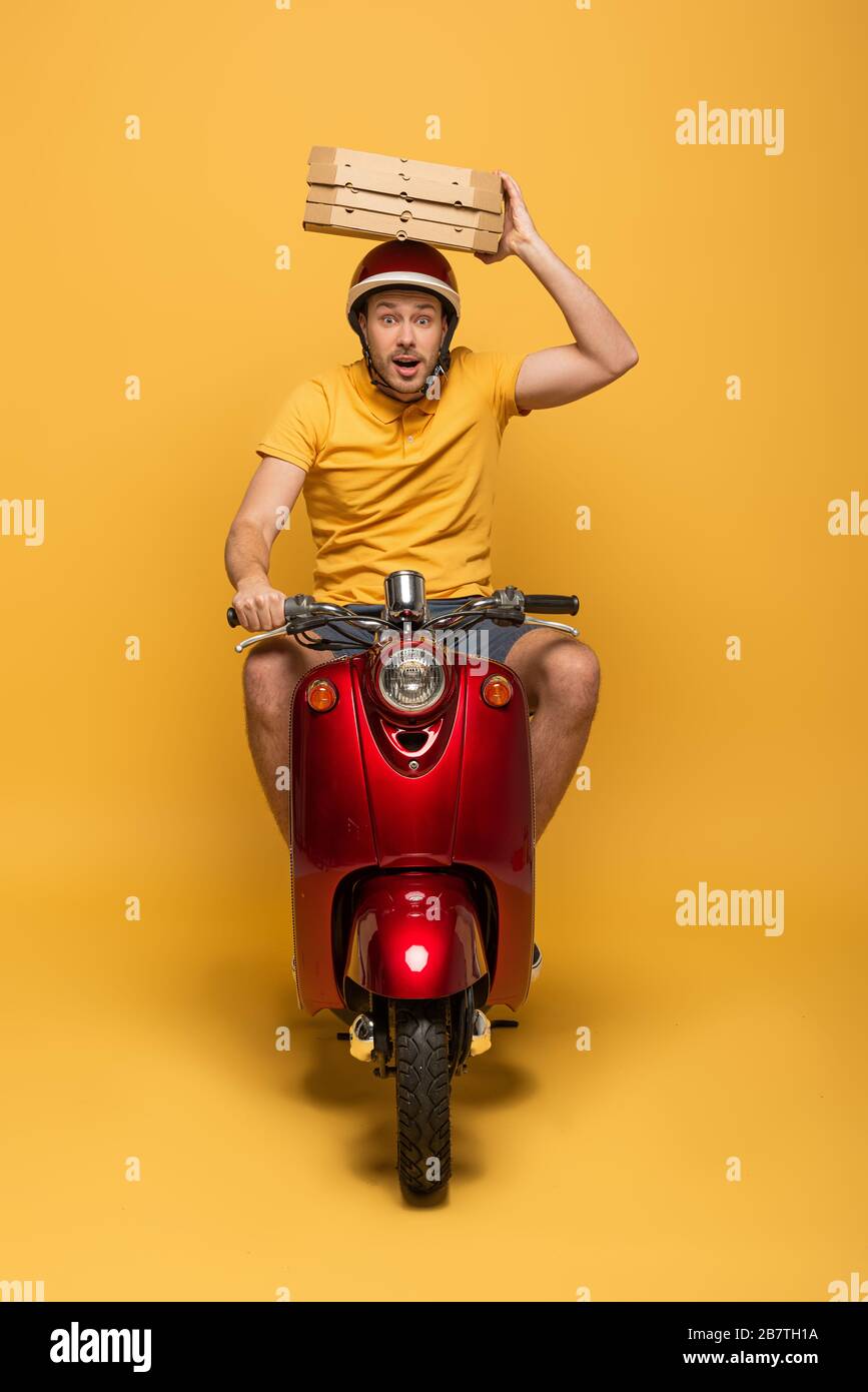 shocked delivery man in yellow uniform riding scooter with pizza boxes ...