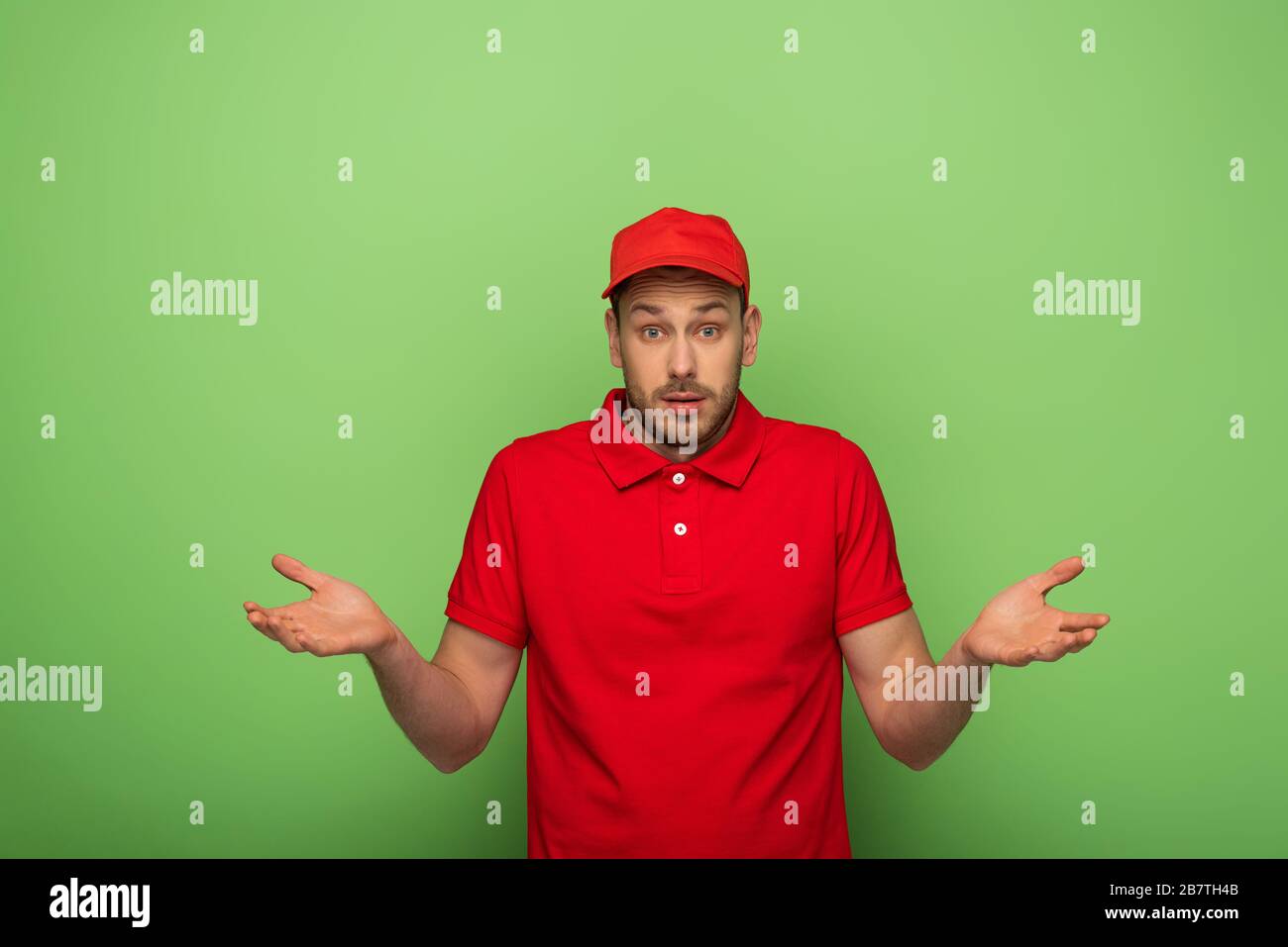 confused delivery man in red uniform showing dubium on green Stock ...