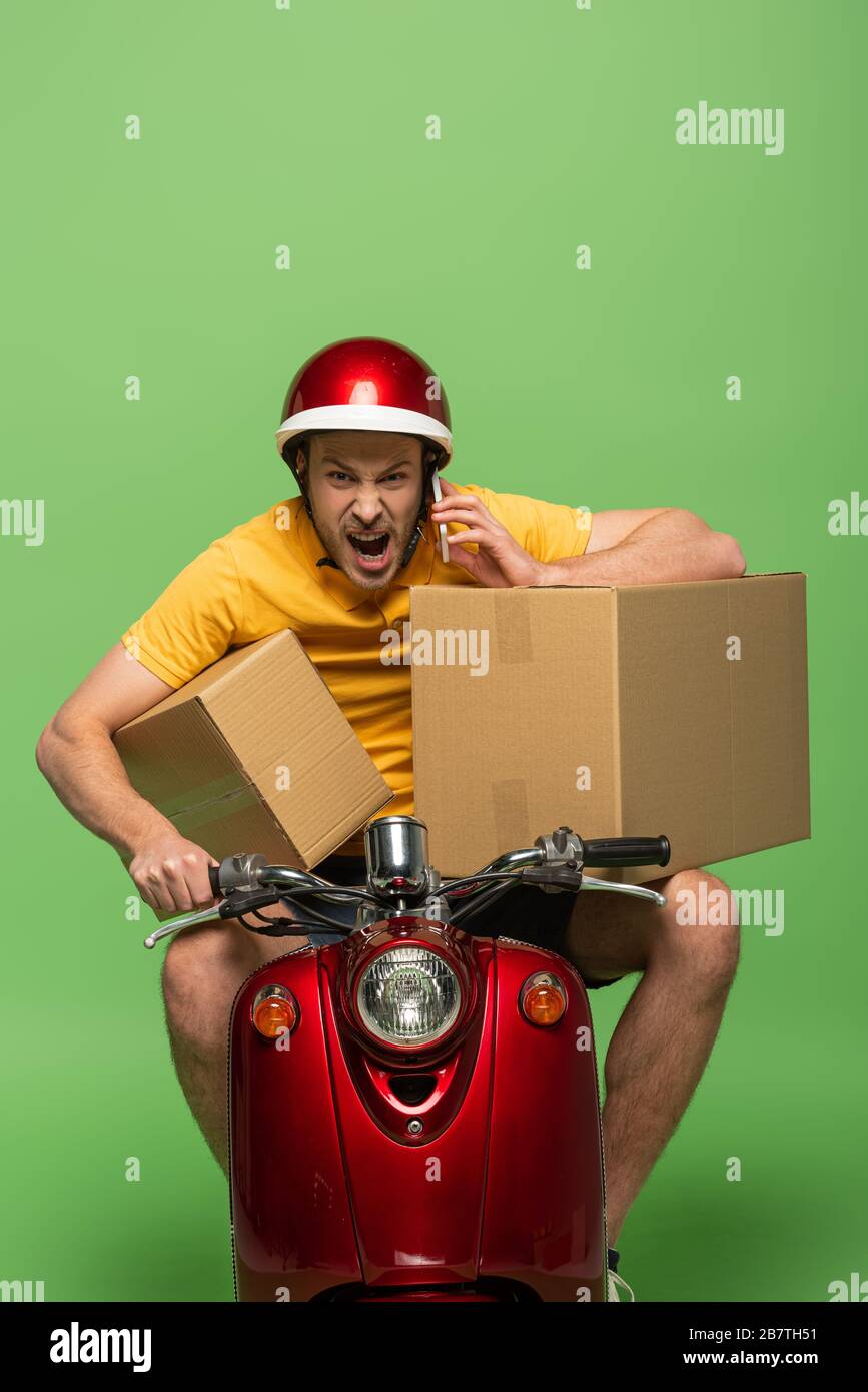 angry delivery man in yellow uniform on scooter with boxes talking on ...