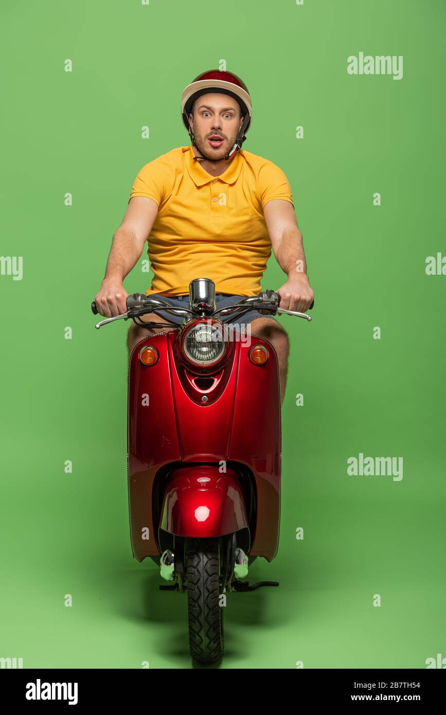 shocked delivery man in yellow uniform and helmet on scooter on green ...